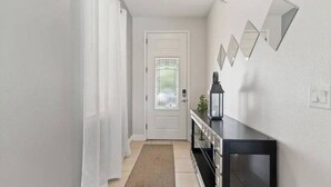 Um corredor com uma porta branca, um aparador preto e um espelho na parede.