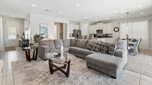 Uma sala de estar moderna com um sofá seccional, uma mesa de centro de vidro e um espaço de jantar com mesa e cadeiras.