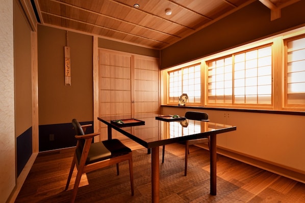 Um quarto japonês tradicional com tatames, portas deslizantes, uma mesa baixa com cadeiras e vista através de um biombos shoji.
