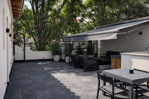 Um pátio com móveis de exterior, espaço para churrasco e plantas em vasos.