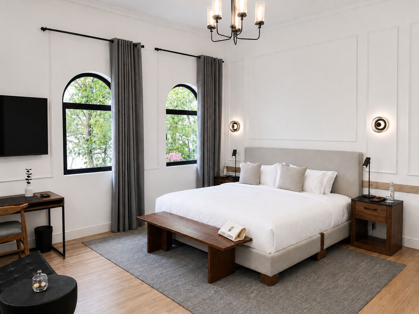 Quarto de hotel moderno com uma cama grande, mesas de cabeceira, escrivaninha, um banco e uma TV.