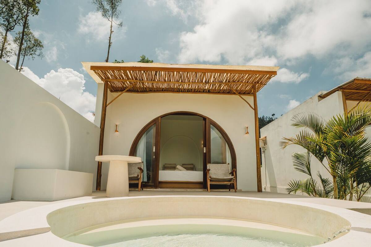 Área de spa com hidromassagem, espaço de estar coberto e quarto com uma grande janela.
