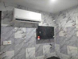 Casa de banho com ar condicionado branco, televisão montada e detector de incêndio na parede.