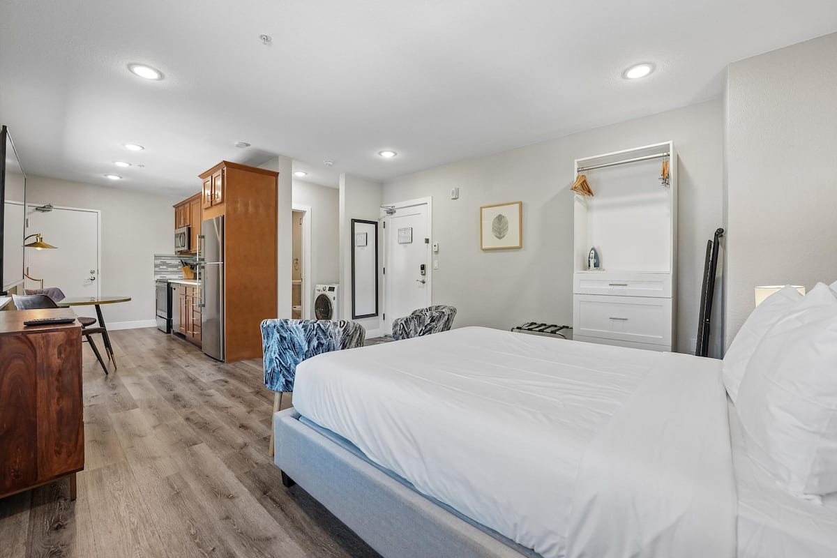Quarto de hotel com cama, escrivaninha, cozinha compacta, banheiro e chuveiro.