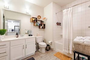 Uma casa de banho moderna com chuveiro, sanita, lavatório e espelho.