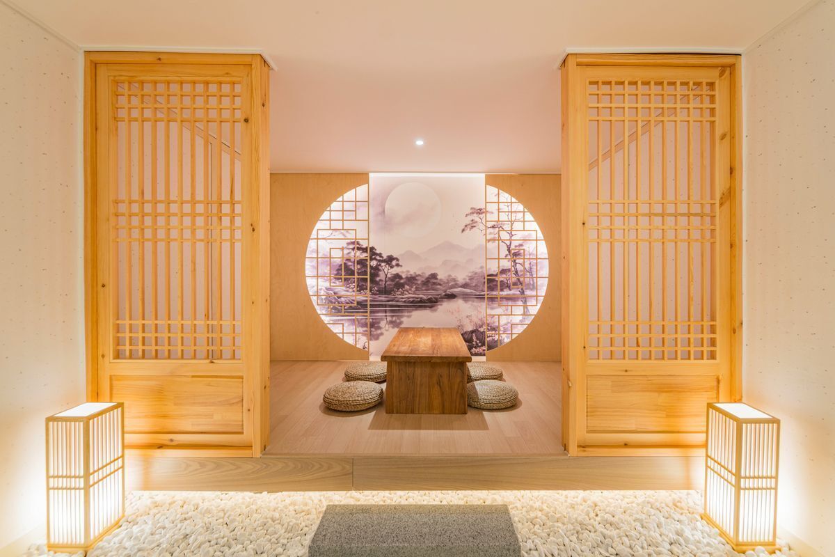 Um quarto japonês tradicional com tatames, uma mesa de madeira e uma grande obra de arte circular na parede.