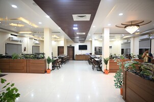 Um espaço amplo e interno com uma mesa comprida, cadeiras, plantas em vasos e um candelabro.