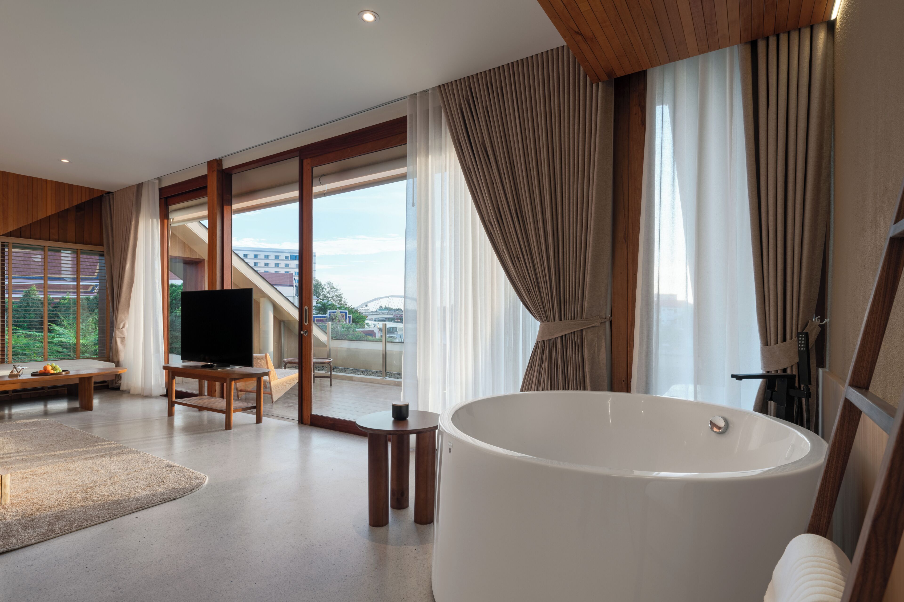 Quarto de hotel moderno com uma banheira grande, televisão de tela plana e vista panorâmica da cidade através de amplas janelas.