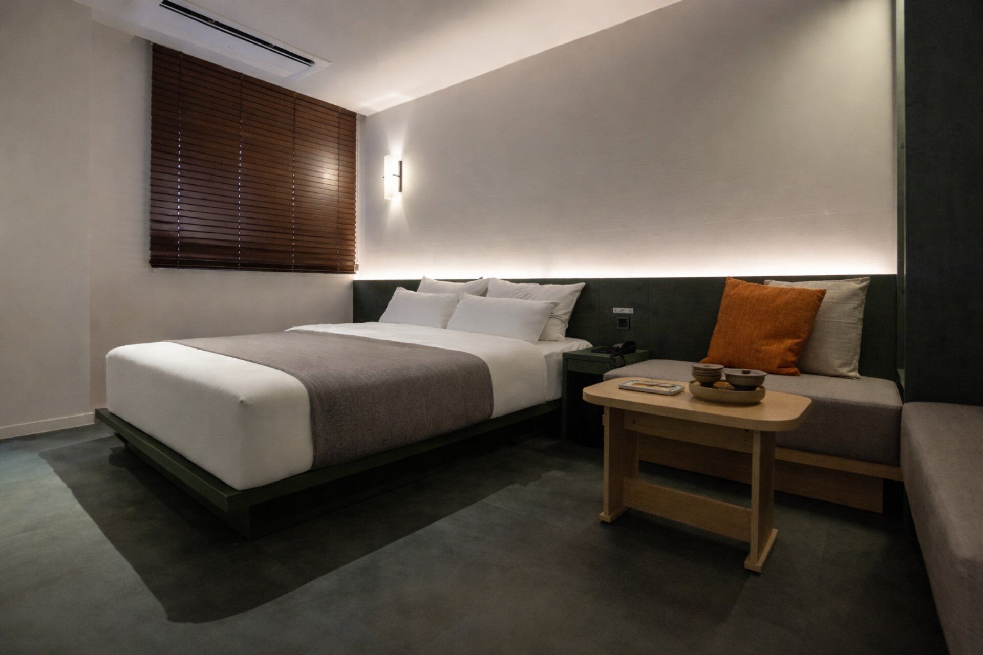 Quarto de hotel moderno com cama, mesa de cabeceira e sofá.