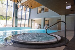 Uma piscina interior moderna com banheira de hidromassagem, janelas amplas e teto de madeira.