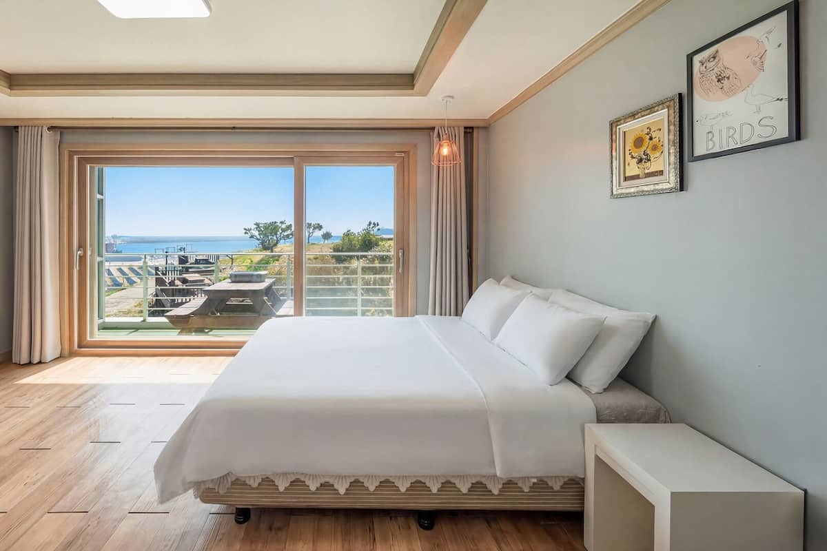 Quarto com uma cama grande, vista para o mar e varanda com móveis de exterior.