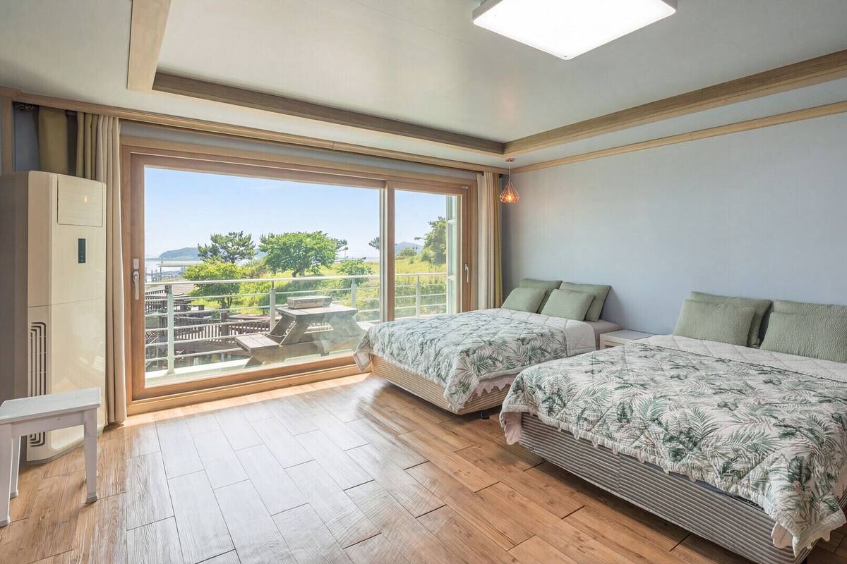 Quarto com duas camas, porta de vidro deslizante para uma varanda e vista para área verde.