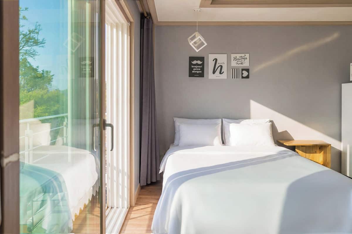 Quarto com cama, mesa de cabeceira, guarda-roupa e vista através de uma porta de vidro.