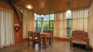 Quarto com teto de madeira, janelas amplas com cortinas, mesa de jantar com cadeiras e um sofá.