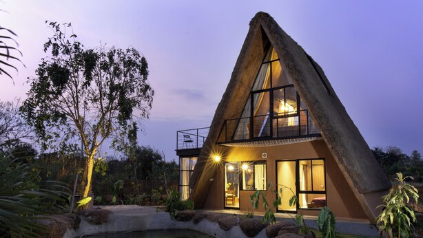 Uma casa com telhado de palha e piscina, cercada por pedras e plantas.