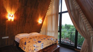 Quarto com cama, paredes de madeira, duas luminárias fixadas na parede, janela com cortinas e um banco.