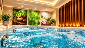 Piscina interior moderna com água cristalina, rodeada por área de spa com plantas e parede de madeira.