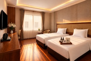 Quarto de hotel com duas camas, uma escrivaninha com cafeteira, televisão e janela com cortinas.