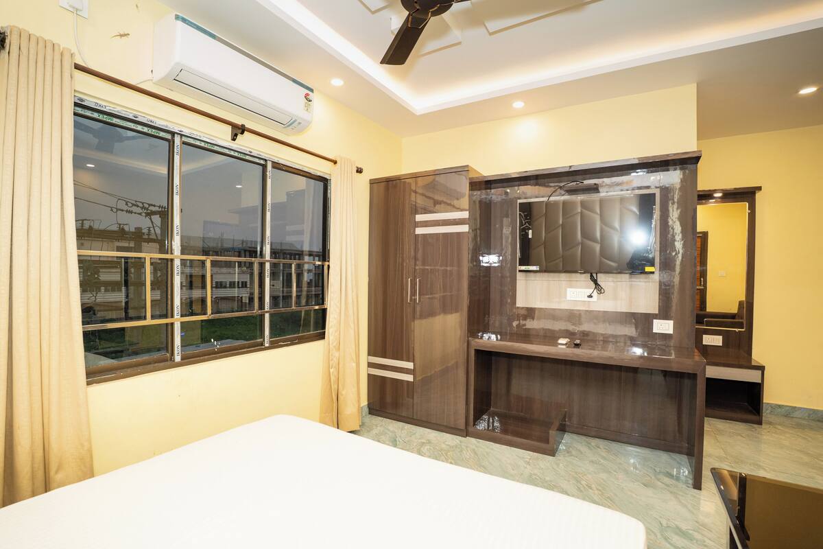 Quarto com cama, guarda-roupa, penteadeira com espelho e janela com cortinas.