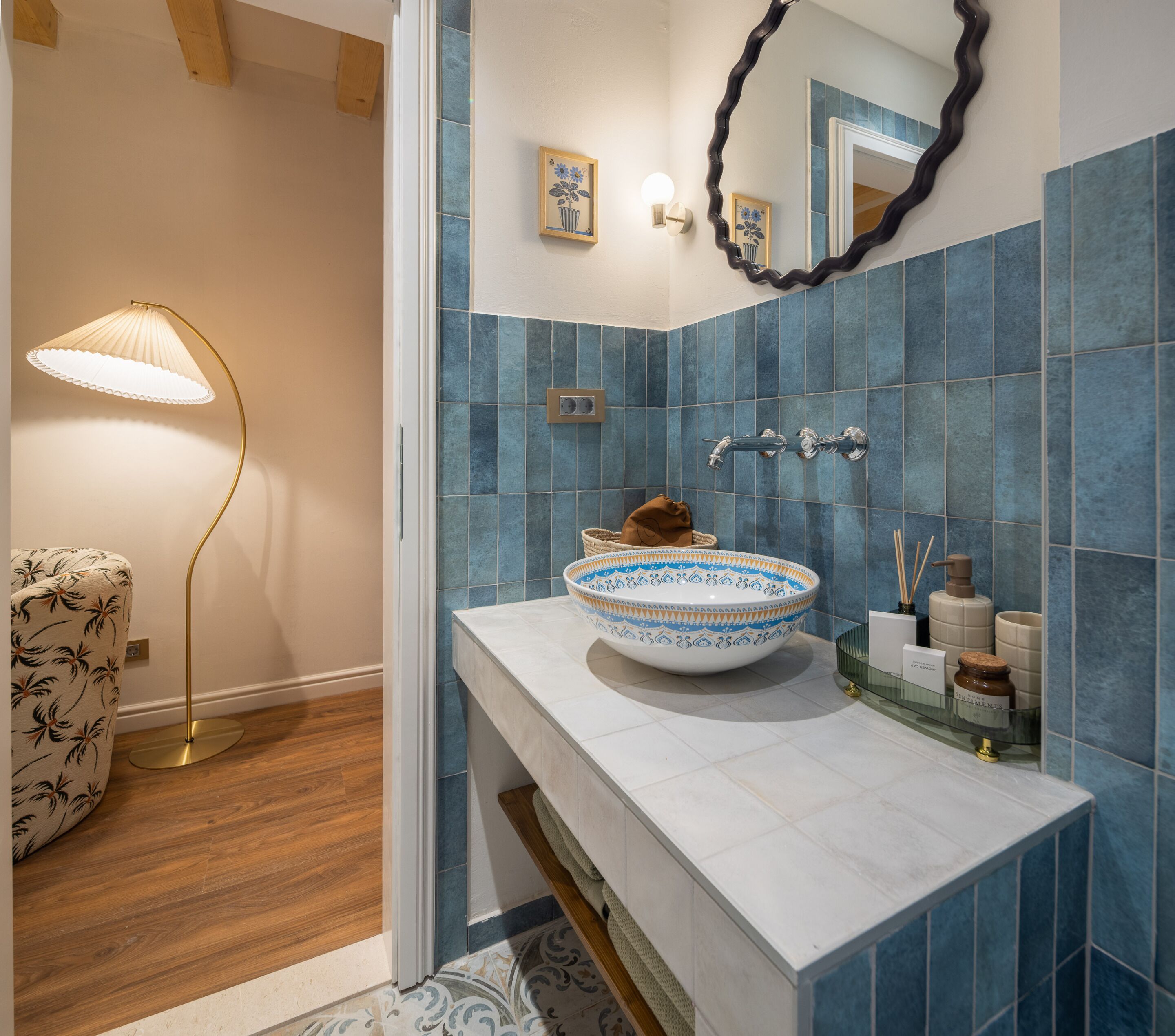 Uma casa de banho com uma bacia grande, azulejos azuis, um espelho e um candeeiro de chão.