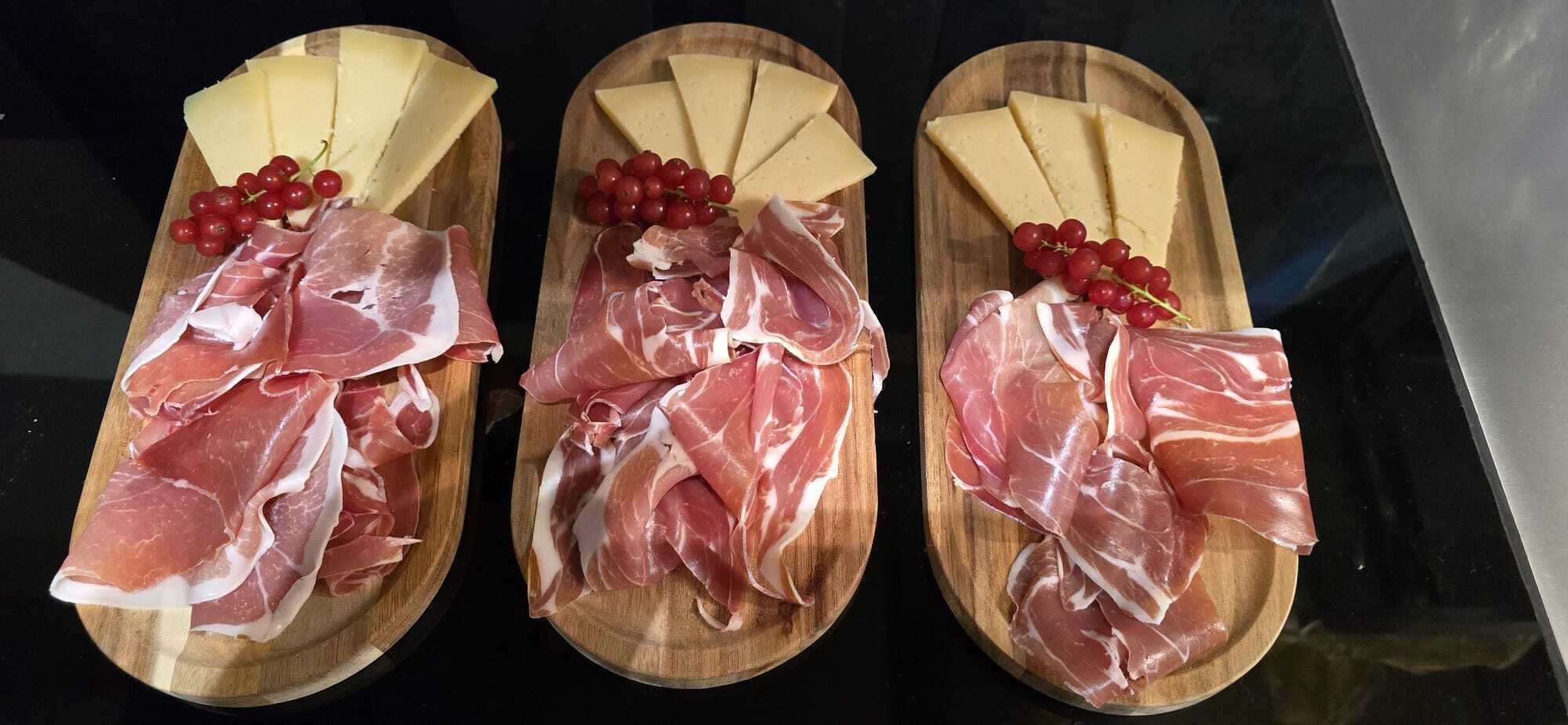 Três tábuas de madeira com presunto fatiado, uvas e queijo.