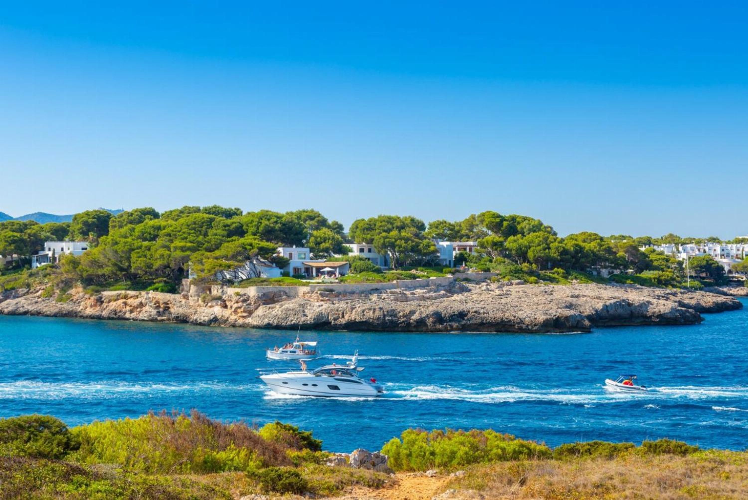 Uma área costeira com barcos na água, casas na margem e terreno rochoso.