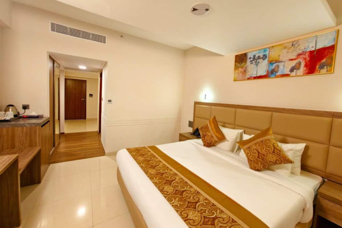 Quarto de hotel com uma cama grande, uma escrivaninha, uma cadeira, uma mesinha de cabeceira e um quadro na parede.