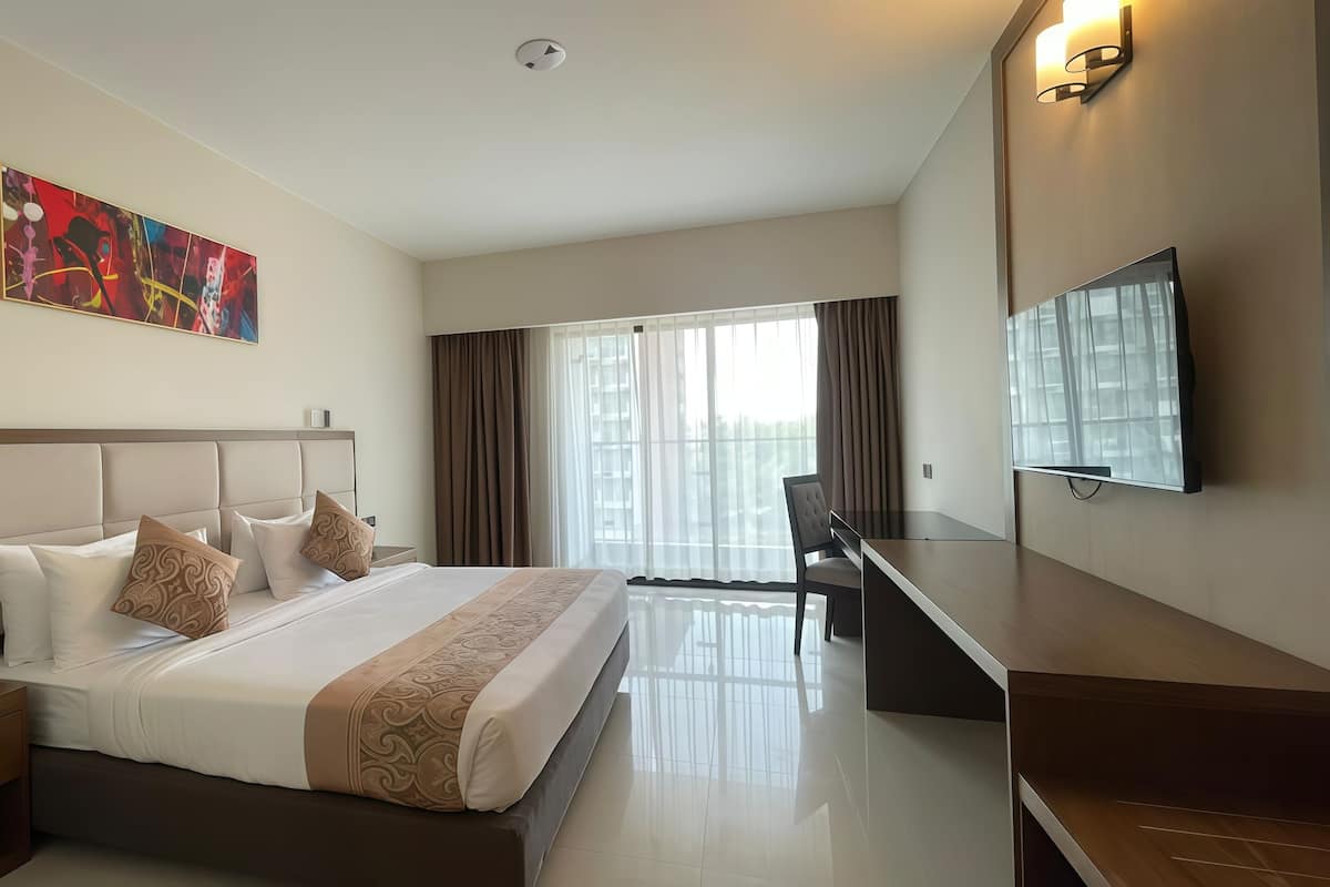 Quarto de hotel com uma cama grande, uma escrivaninha, uma televisão de tela plana, um quadro na parede e vista para o exterior pela janela.