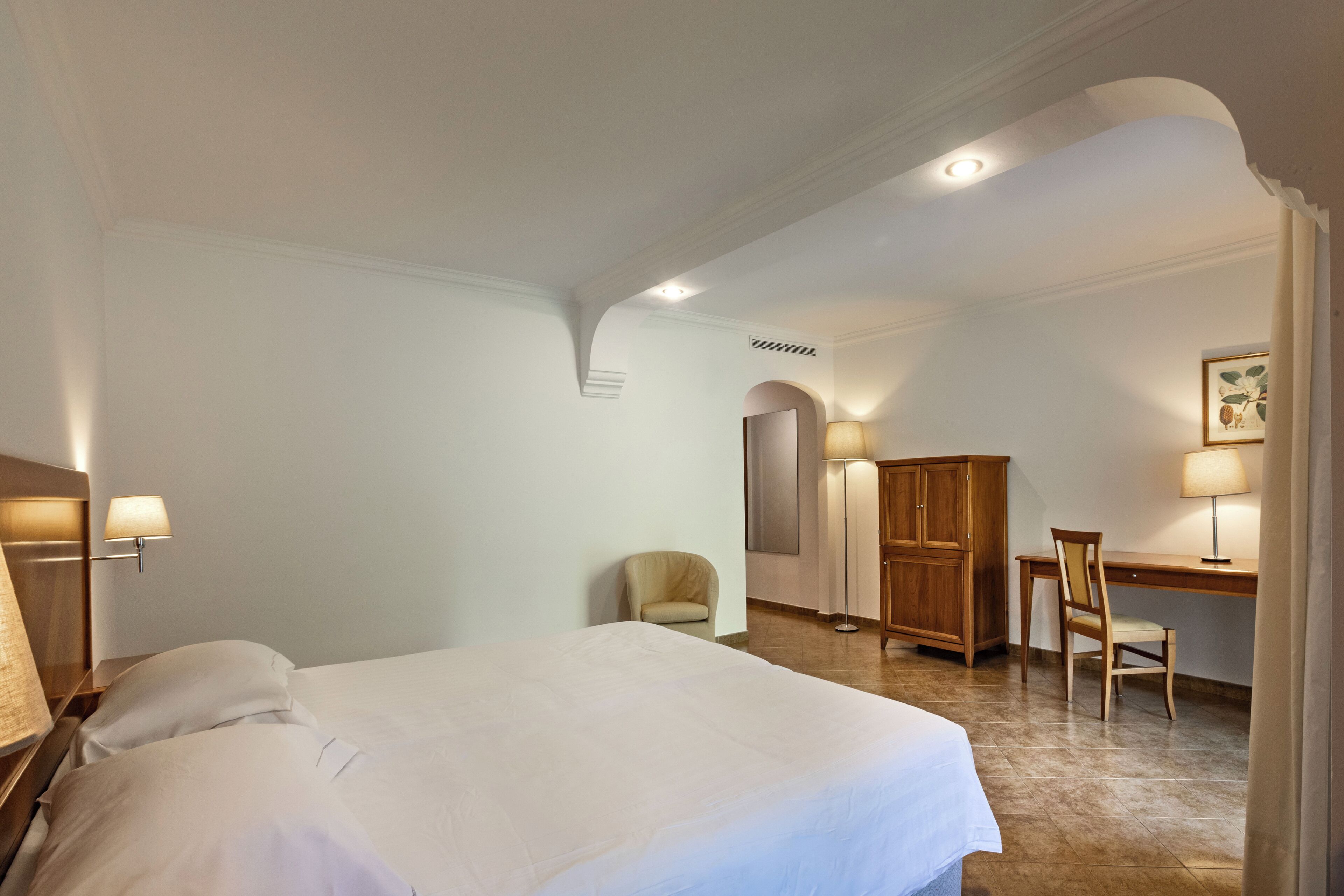 Quarto de hotel com cama, escrivaninha, cadeira e guarda-roupa.