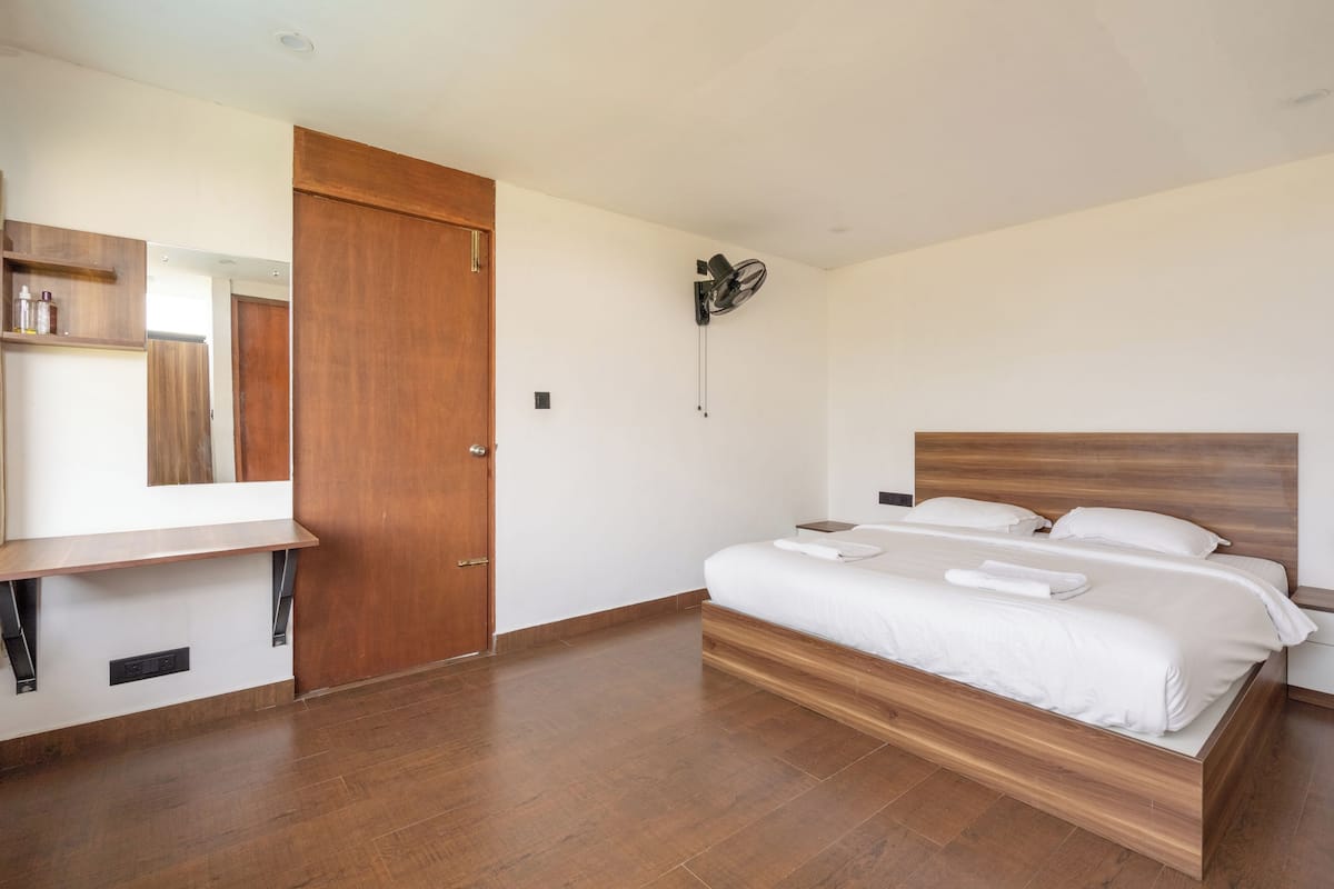 Quarto com cama de madeira, mesa de cabeceira, espelho e porta.