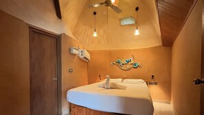Um quarto com cama de madeira, ventoinha no teto, ar condicionado fixado na parede e um objeto decorativo na parede.