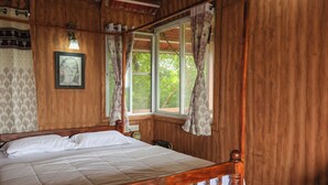 Uma cama com estrutura de madeira, roupa de cama branca, um quadro na parede e uma janela com cortinas.