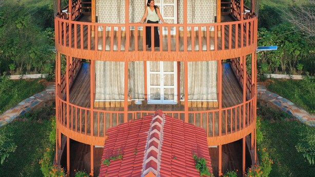 Uma casa de madeira de dois andares com telhado vermelho, varanda e um caminho de pedra que leva à entrada.