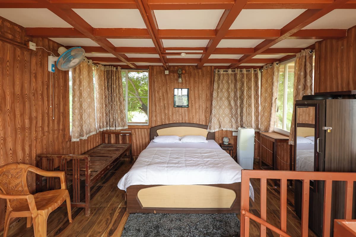 Quarto de madeira com uma cama, uma escrivaninha, uma cadeira e um ventilador.