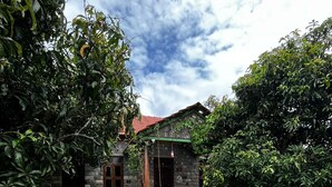 Um edifício de pedra com telhado vermelho, rodeado por vegetação exuberante e um caminho de pedra.
