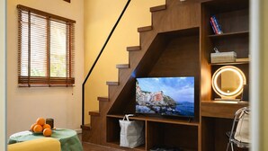 Uma sala de estar moderna com escada de madeira, TV de tela plana, espelho redondo e uma mesa com laranjas.