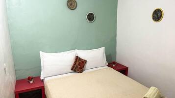 Quarto com cama, duas mesas de cabeceira, uma mesinha lateral vermelha e pratos decorativos na parede.