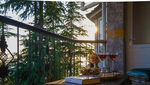 Varanda com vista para árvores, uma mesa com um livro, um vaso com flores e dois copos de martini.