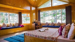 Interior de uma cabana de madeira com cama, área de estar e grandes janelas.