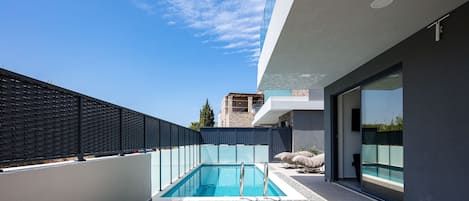 Piscina no terraço com espreguiçadeiras, estrutura de vidro e um edifício moderno ao fundo.