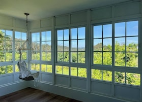 Quarto com janelas amplas, uma cadeira suspensa e vista para o verde.