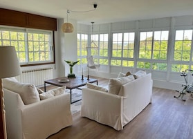 Um quarto espaçoso com uma grande janela, um conjunto de sofás, uma mesa de centro e uma cadeira suspensa.