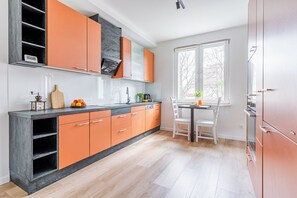 Uma cozinha moderna com armários cor de laranja, bancada preta e janela com vista para árvores.