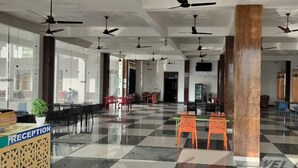 Um hall amplo com piso xadrez, várias ventoinhas no teto e um balcão de recepção.
