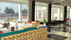 Uma área de recepção com balcão de check-in, mesa de atendimento e vista para o exterior.