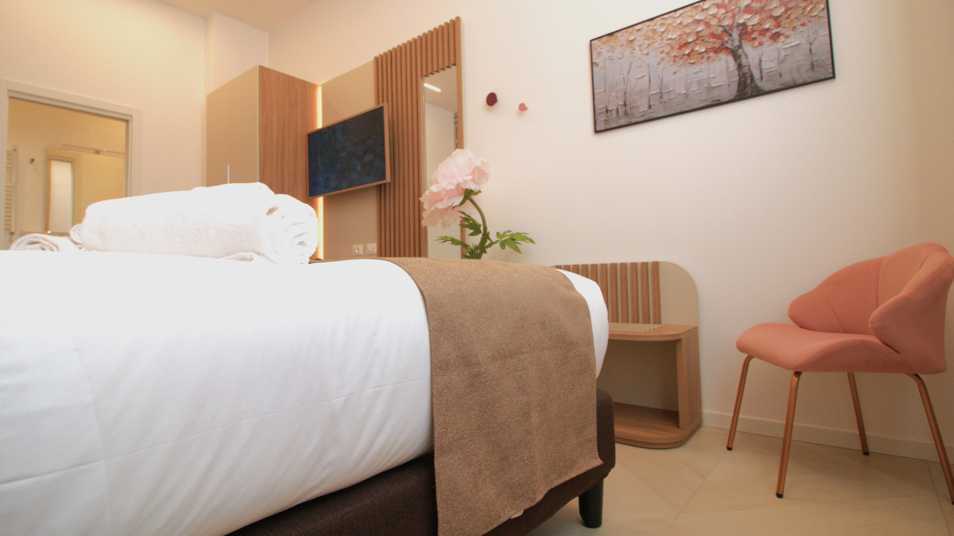 Quarto de hotel com cama, cadeira, escrivaninha, espelho e um quadro na parede.