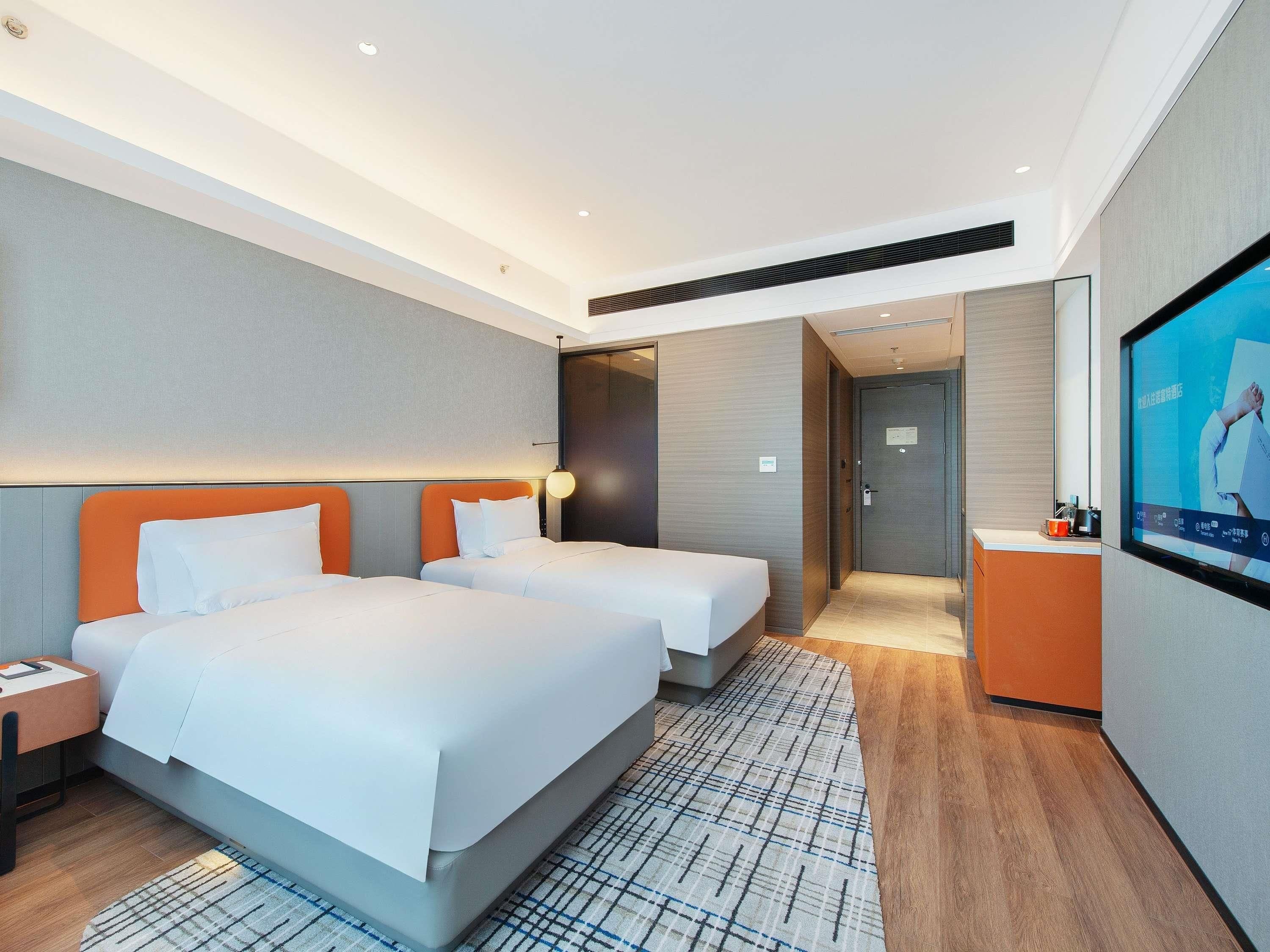 Quarto de hotel com duas camas, uma escrivaninha, televisão e área de recepção.