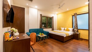 Quarto de hotel com cama, sofá, escrivaninha com lanches, cadeira e janela com cortinas.