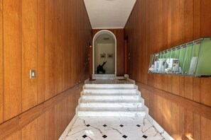 Uma escadaria de mármore com painéis de madeira nas paredes, que leva a um quarto com parede verde e um mural de avisos.