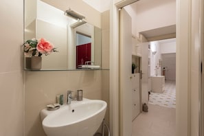 Casa de banho com lavatório branco, espelho e um vaso com flores.